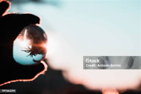 크리스탈 유리 공을 들고 장갑을 낀 손으로 아침에 거친 태양이 공에 반사 밝은 푸른 하늘의 색조입니다 유리 공 내부의 깊은 초점 개념에 대한 스톡 사진 및 기타 이미지