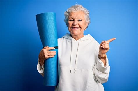 시니어 아름다운 스포티 한 여자 들고 매트 용 요가 서 위에 고립 된 파란색 배경 매우 행복 가리키는 손과 손가락 으로 측면에 가리키기에 대한 스톡 사진 및 기타 이미지