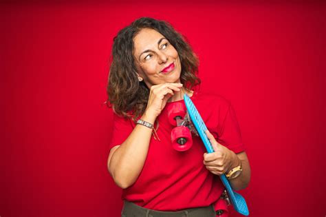 빨간 고립 된 배경 심각한 얼굴 을 통해 스케이트 보드를 들고 중년 시니어 스케이터 여자 질문에 대 한 생각 매우 혼란 스러운 아이디어 개념에 대한 스톡 사진 및 기타