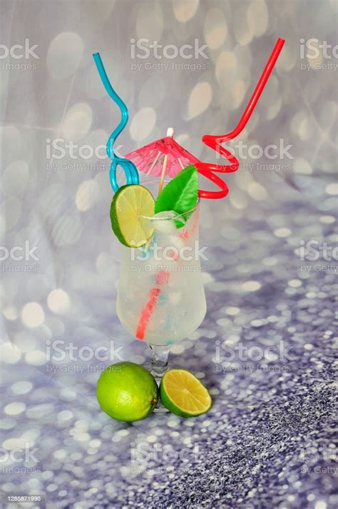 얼음이 있는 라임 주스의 키가 큰 유리와 빨대와 우산을 곁들인 감귤류 한 조각 회색 추상적 배경의 이국적인 녹색 과일 근처