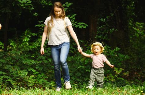 화창한 늦은 여름날 공원에서 산책을 즐기는 태양 모자를 쓴 귀여운 건방진 20 개월 된 유아는 엄마와 손을 잡고 달리면서 얼굴에 약간 충격적인 표정을 짓고 있습니다 2 3