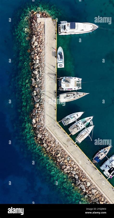 Aerial View Of Luxury Yachts And Boats Moored Along Curved Stone Breakwater With Turquoise