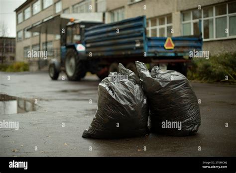 Two Bags Of Garbage On Background Of Tractor Garbage Collection On Site Garbage Bags On Road