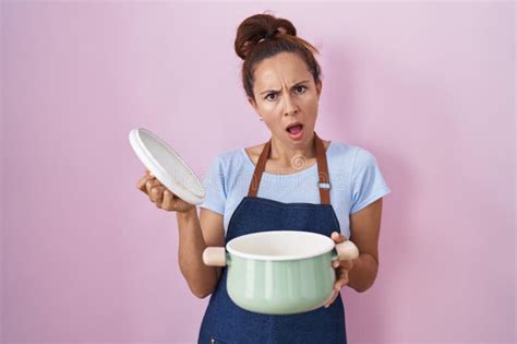 Brunette Woman Wearing Apron Holding Cooking Pot In Shock Face Looking