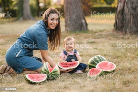 데민 드레스를 입은 엄마와 딸은 여름 공원에서 수박을 먹는다 아기 소녀는 잔디에 앉아있다 행복한 가족이 함께 시간을 보낸다 가족에 대한 스톡 사진 및 기타 이미지 Istock