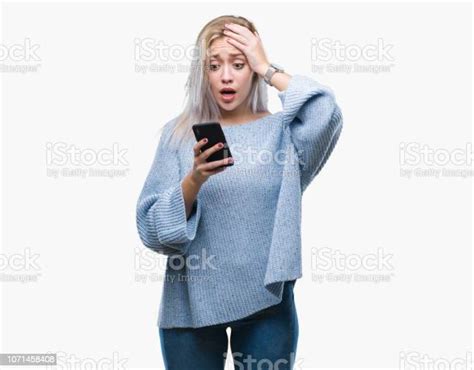손으로 머리에 압박 절연된 배경 위에 스마트폰을 사용 하 여 메시지를 보내는 젊은 금발의 여 자가 문자 충격 수치심과 깜짝 얼굴로 분노와 좌절 두려워 하 고 실수에 대 한
