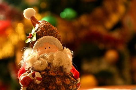 겨울 방학 전에 집 안에서 볼 수 있는 풍성하게 장식된 크리스마스 트리 옆에 있는 나무 테이블에 모직 상단이 있는 빨간 모자를 쓴 산타클로스의 작은 점토 인형을 가까이서