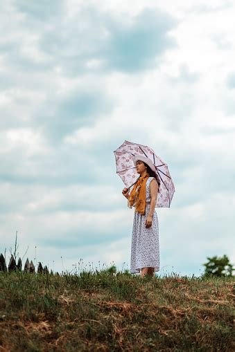 밀짚 모자를 쓰고 옷을 입은 한 젊은 여성이 우산을 손에 들고 언덕 위에 서 있다 배경에 흐린 하늘 세로 심리학의 개념 가을에