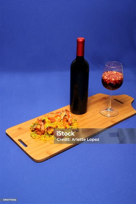 사프란 조개류 새우 및 야채로 만든 발렌시아 스페인의 전통 빠에야 쌀은 레드 와인과 파란색 배경에 클레리코트 한 잔과 함께 나무 판에 제공됩니다 Clericot에 대한 스톡