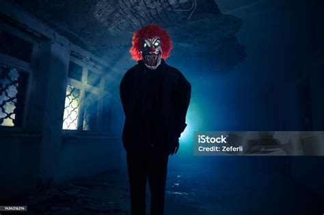 빨간 머리카락과 하얀 눈을 가진 무서운 사악한 광대의 클로즈업 관찰자를 쳐다 보며 그 앞에 빨간 풍선이 있고 검은 배경에 대해 어릿광대 서커스 공연자에 대한 스톡 사진 및