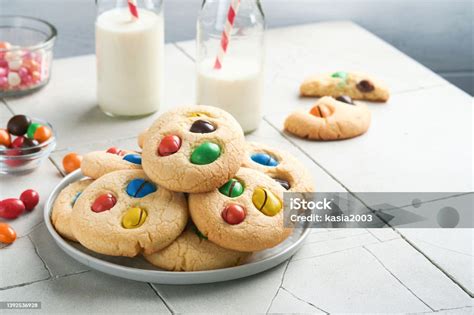 다채로운 초콜릿 사탕과 우유로 만든 수제 쿠키 밝은 회색 배경에 우유 병이있는 접시에 여러 가지 색의 사탕이있는 쇼트 브레드 쿠키가 쌓여 있습니다 이유식 개념 공간을
