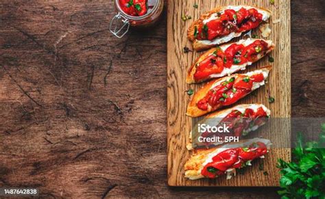 크림 치즈를 곁들인 밀 브루스케타와 올리브 오일에 구운 빨간 파프리카 나무 식탁 배경에 있는 소박한 나무 도마에 허브가 제공됩니다 가을에 대한 스톡 사진 및 기타 이미지