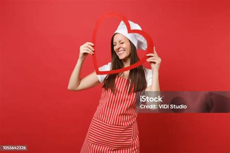 주부 여성 요리사 요리사 또는 줄무늬 앞치마 흰색 티셔츠 모자 요리사 모자 빨간 벽 배경에 고립 된 베이커 가 정부 여 자가