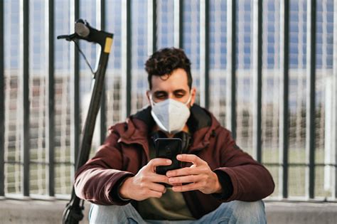 얼굴 마스크를 가진 잘생긴 남자는 자신의 전기 스쿠터에 앉아 자신의 휴대 전화와 메시지를 보내는 전화에 집중합니다 30 34세에 대한 스톡 사진 및 기타 이미지 Istock