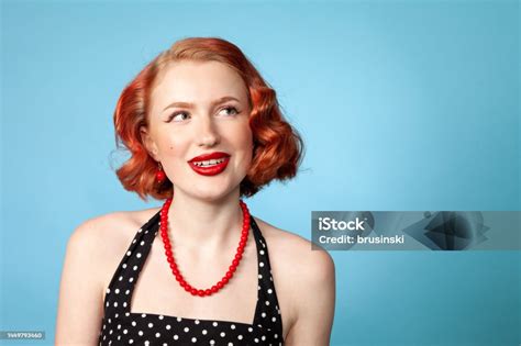 파란색 배경에 물방울 무늬 드레스를 입고 복고풍 스타일로 옷을 입은 쾌활한 빨간 머리 백인 여성의 스튜디오 초상화 복고풍에 대한 스톡 사진 및 기타 이미지 Istock