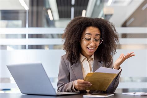 사무실의 책상에 앉아서 편지가 든 봉투를 열고 놀라서 손을 벌리고 메시지를 읽는 행복한 젊은 아프리카계 미국인 여성 경영자에 대한 스톡 사진 및 기타 이미지 Istock