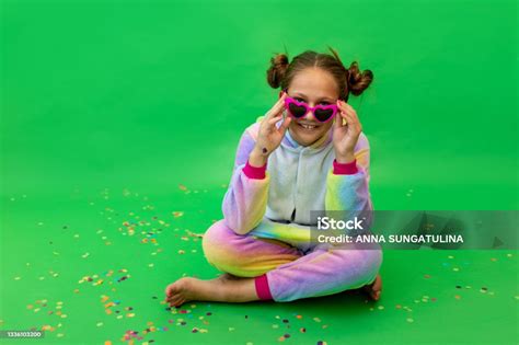 어린 소녀가 밝은 양복과 안경을 쓴 스트리머와 함께 녹색으로 고립된 배경에 앉아 있습니다 텍스트 공간입니다 휴일 생일 및 판매의 개념 10 11세에 대한 스톡 사진 및 기타