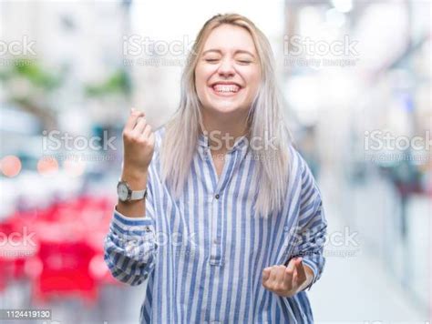 젊은 금발 여자 격리 된 배경에 매우 행복 하 고 흥분 무기와 우승자 제스처를 하 고 웃 고 성공을 위한 비명 축 하 개념입니다