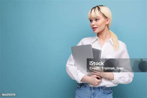 흰 셔츠와 청바지를 입은 짧은 머리를 한 젊은 금발의 백인 여성은 복사 공간을 배경으로 업무용 노트북과 노트북을 들고 있다 사업