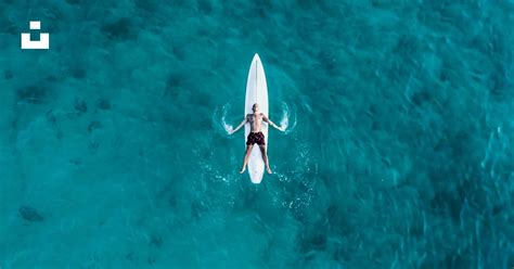 남자는 해변에서 흰색 서핑 보드에 누워있는 보드 반바지를 입고 있습니다 사진 Unsplash의 무료 파랑 이미지