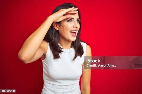 빨간 고립 된 배경 위에 서있는 흰색 드레스를 입은 젊은 아름다운 여성은 매우 행복하고 머리 위로 손으로 멀리 보고 미소 개념 검색 거리가 먼에 대한 스톡 사진 및 기타