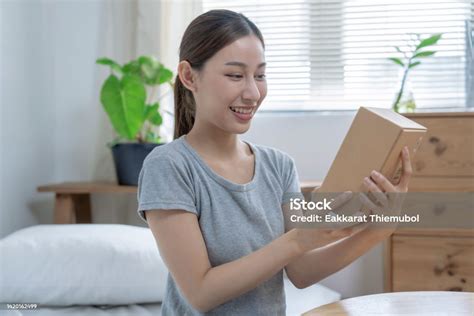 아시아 여성이 흥분하여 소포 상자를 열고 그녀는 소포 상자에있는 물건을보고 행복한 표정을 보여주었습니다 가정 생활에 대한 스톡