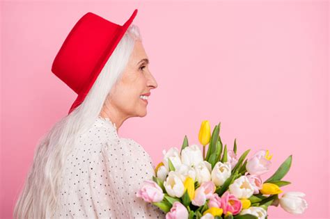 핑크 파스텔 컬러 배경에 고립 된 튤립 플로리스트 숍을 들고 매력적인 쾌활한 회색 머리 할머니의 프로필 측면 보기 초상화 금발