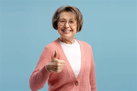 엄지 손가락을 치켜 올리는 제스처를 보여주고 카메라를보고 푸른 배경에 미소 짓는 행복한 노인 여성 70 79세에 대한 스톡 사진 및 기타 이미지 Istock