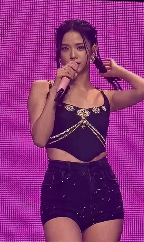 A Woman In Black Shorts And Crop Top Holding A Microphone To Her Mouth While Standing On Stage