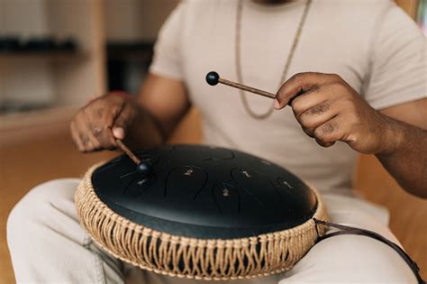 막대기를 사용하여 포도창으로 전통 민족 음악을 연주하는 알아볼 수 없는 영적인 아프리카 남자가 연꽃 자세로 바닥에 앉아 있는 모습의 자른 사진 35 39세에 대한 스톡 사진