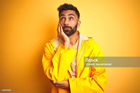 고립 된 노란색 배경 위에 서있는 비옷을 입은 젊은 인도 남자는 피곤하고 교차 된 팔로 우울증 문제로 지루해 보입니다 가을에 대한 스톡 사진 및 기타 이미지 Istock