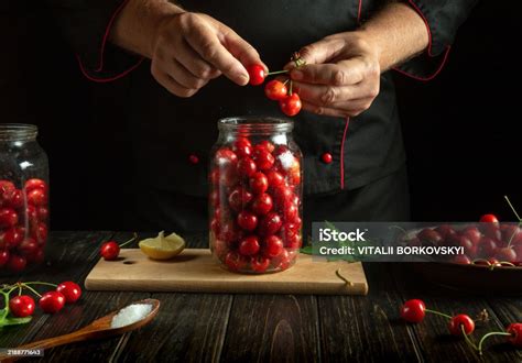 솜씨 좋은 요리사가 따뜻하고 소박한 주방에서 항아리와 신선한 재료에 둘러싸여 가장 잘 익은 과일을 선택하여 보존을 위해 체리를 조심스럽게 준비합니다 Diy에 대한 스톡 사진