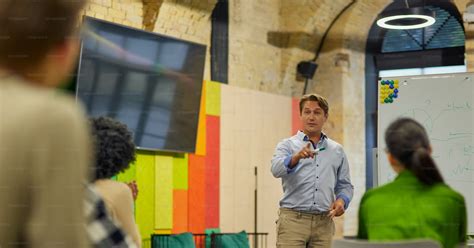 팀 빌딩 교육 자신감 있는 남성 비즈니스 코치 또는 연사가 현대 사무실의 책상에 앉아 있는 다인종 그룹에 맞서 연설을 합니다 교육 및 비즈니스 사진 Unsplash의