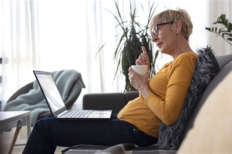 짧은 금발 머리를 가진 나이 든 여자 는 거실에 소파에 앉아 화상 채팅을 통해 노트북에 친구와 채팅 55 59세에 대한 스톡 사진 및 기타 이미지 Istock
