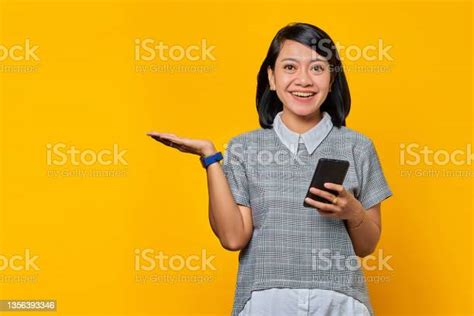 손바닥에 복사 공간을 보여주고 노란색 배경에 휴대 전화를 들고 미소 젊은 여성의 초상화 25 29세에 대한 스톡 사진 및 기타 이미지 25 29세 Brand Name