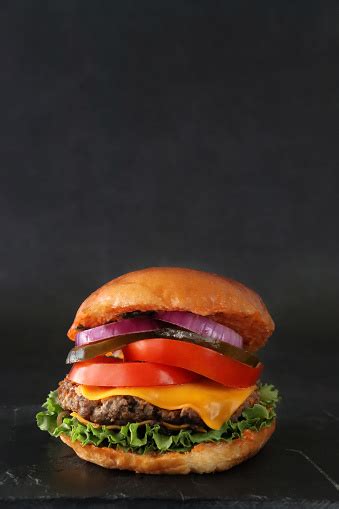빵 롤빵 햄버거 패티 녹는 가공 치즈 조각 양상추 잎 얇게 썬 토마토 피클과 붉은 양파 조각 검은 배경 전경에 초점 복사 공간에