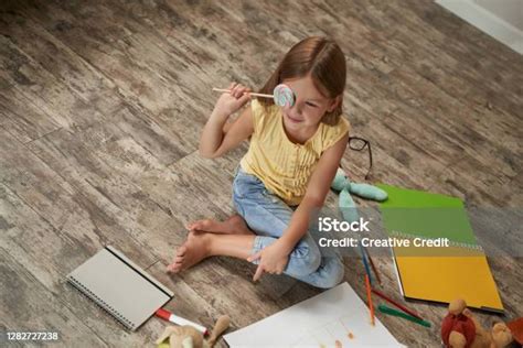 집에서 그녀의 방에있는 나무 바닥에 앉아있는 동안 롤리팝을 들고 미소 귀여운 작은 백인 소녀 그녀는 장난감과 화려한 연필로