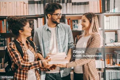 도서관에 서 있고 학교 프로젝트에 필요한 책을 들고 있는 세 명의 쾌활 한 학생 책이 있는 배경 선반 교육에 대한 스톡 사진 및