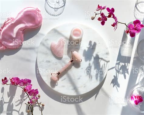 핑크 쿼즈 페이스 롤러 대리석 접시에 보습 크림 핑크 슬립 마스크 몬스터 나뭇잎과 활기찬 마젠타 난초 꽃이국적인 플랫 누워 햇빛 긴 그림자 얼굴 마사지 0명에 대한 스톡