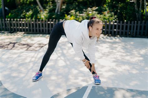 운동 루틴에 관여 하는 어두운 머리 운동 유럽 여자의 수평 샷 야외 착용 활동적인 복 미소 긍정적으로 따뜻하게 열차 근육 전체