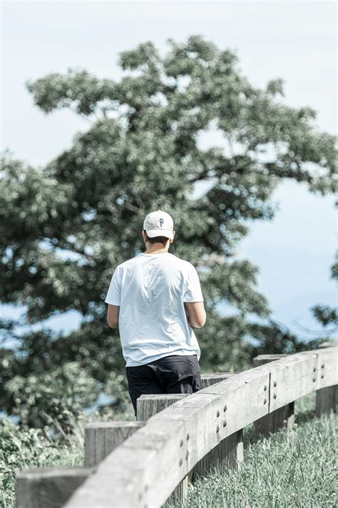 흰색 티셔츠와 파란색 데님 청바지를 입은 남자가 갈색 나무 위에 서 있는 흰색 모자를 쓰고 있다 사진 Unsplash의 무료 사람의 이미지