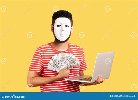 Anonymous Rich Hacker Or Programmer Man Hiding Face With White Mask Working On Laptop Showing