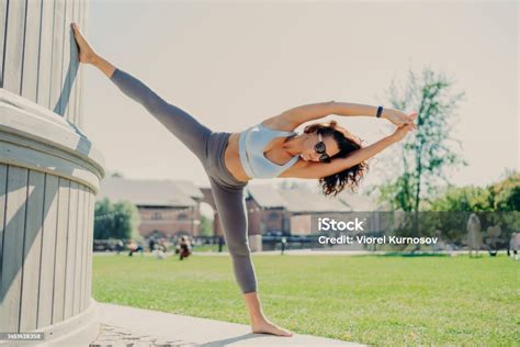 유연한 맞는 여자의 수평 샷은 좋은 신체 모양으로 팔을 제기 와 한쪽 다리 에 서 체조 운동은 야외에서 좋은 날씨를 즐긴다 사람