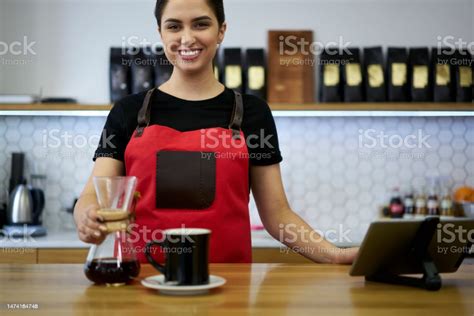 아로마 커피 음료를 만들기 위해 유리 필터를 사용하는 카페의 바에 서 있는 제복을 입은 쾌활한 백인 여성 20대 바리스트의 절반 길이 초상화 항아리와 머그잔을 사용하여 웃고