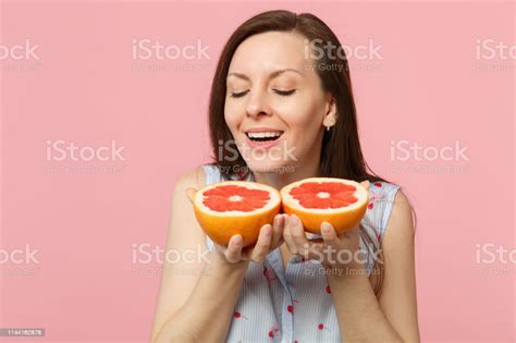 스튜디오에서 분홍색 파스텔 벽 배경에 고립 된 신선한 잘 익은 자 몽의 두 Halfs를 들고 여름 옷에 젊은 여자를 웃는 사람들은 생생한 라이프 스타일 휴식 휴가 개념입니다