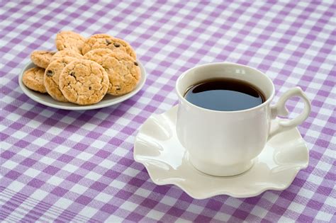 물결 모양의 가장자리와 귀리 쿠키가 있는 접시에 차를 가진 도자기 컵은 체크 무늬의 흰색 보라색 식탁보에 다크 초콜렛 조각이 있습니다 0명에 대한 스톡 사진 및 기타 이미지