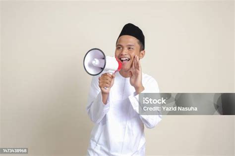 해골 모자를 쓴 흰 셔츠를 입은 매력적인 아시아 무슬림 남자의 초상화는 메가폰을 사용하여 더 크게 말하며 제품을 홍보합니다 광고 개념입니다 회색 배경에 격리된 이미지 20