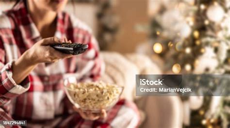 잠옷 차림의 여성이 크리스마스 연휴 동안 한 손에는 Tv 리모컨을 다른 한 손에는 팝콘 한 그릇을 들고 있습니다 12월에 대한 스톡 사진 및 기타 이미지 Istock