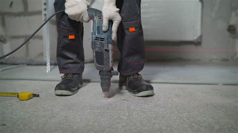 그는 콘크리트 또는 돌 표면에 플라스틱 바닥 베이스의 설치 및 설치 기술 마스터는 펀치로 바닥에 구멍을 뚫습니다 한 작업자가 망치 드릴로 바닥을 뚫습니다 T 드릴에 대한