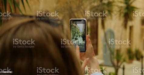 뒤에서 볼 수 있는 여자는 카메라 응용 프로그램에서 화면의 셔터 버튼을 눌러 전화를 받습니다 여성의 클로즈업 샷은 스마트폰 사진 앱을 사용하여 이국적인 거리의 사진을